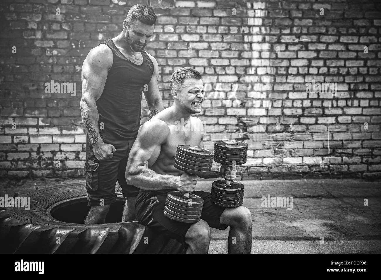 Two muscular athletes training, one raise, push the barbbell when other ...