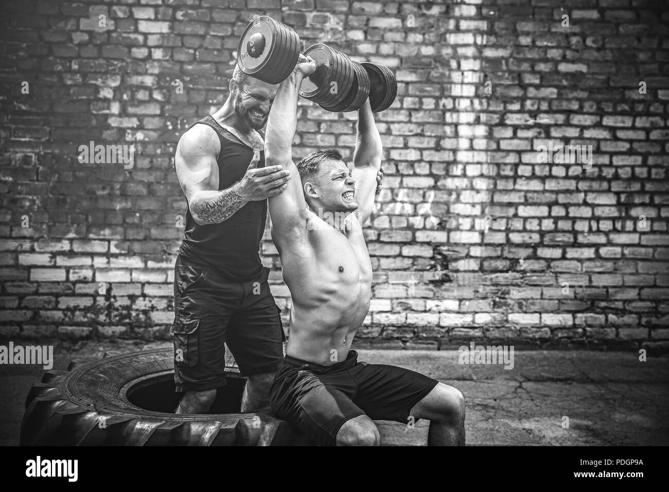 Two muscular athletes training, one raise, push the barbbell when other ...