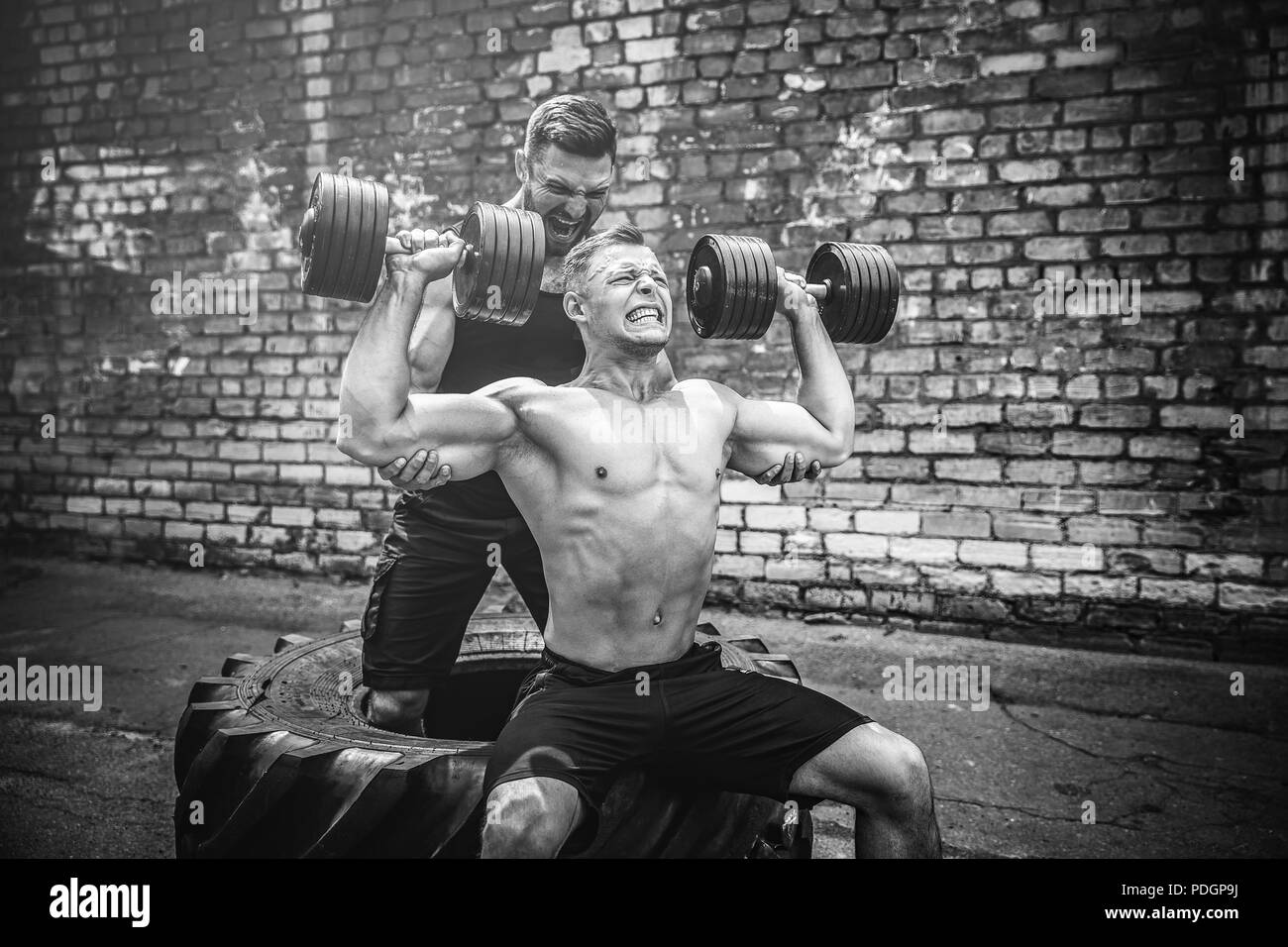 Two muscular athletes training, one raise, push the barbbell when other ...