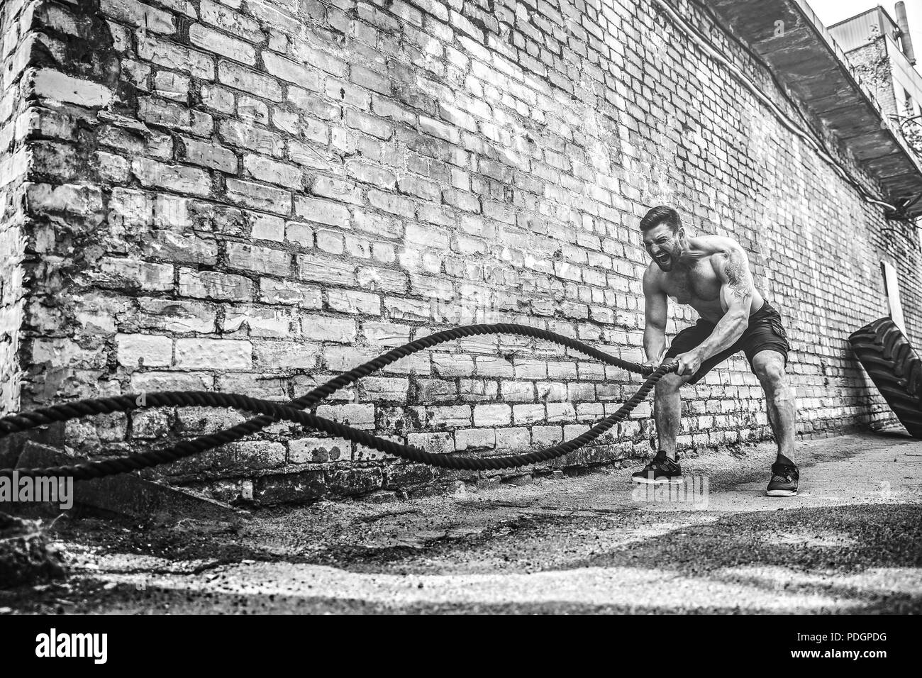 Athletic man working out with rope in front of brick wall. Strength and ...