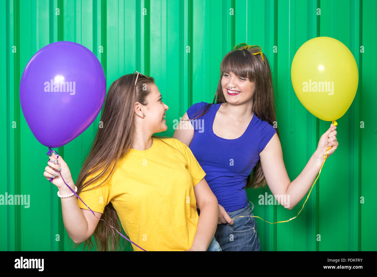 Happy girls with helium balloons on green wall Stock Photo - Alamy