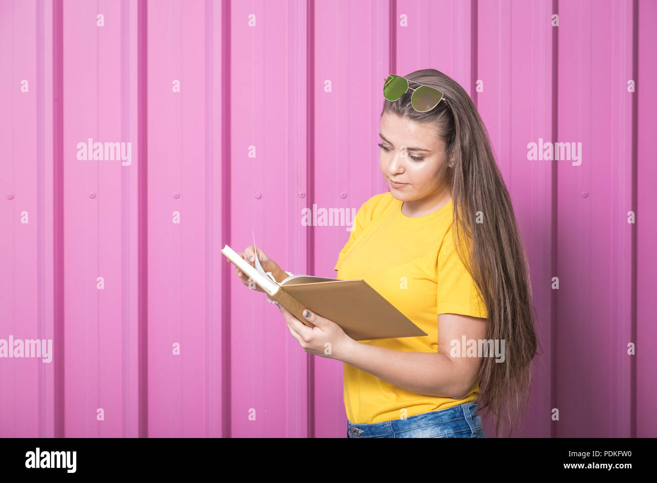 Beautiful young woman reading a book isolated on pastel pink background ...