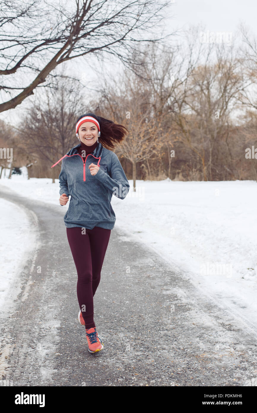 Portrait of Caucasian young woman jogging outside in winter park. Girl ...