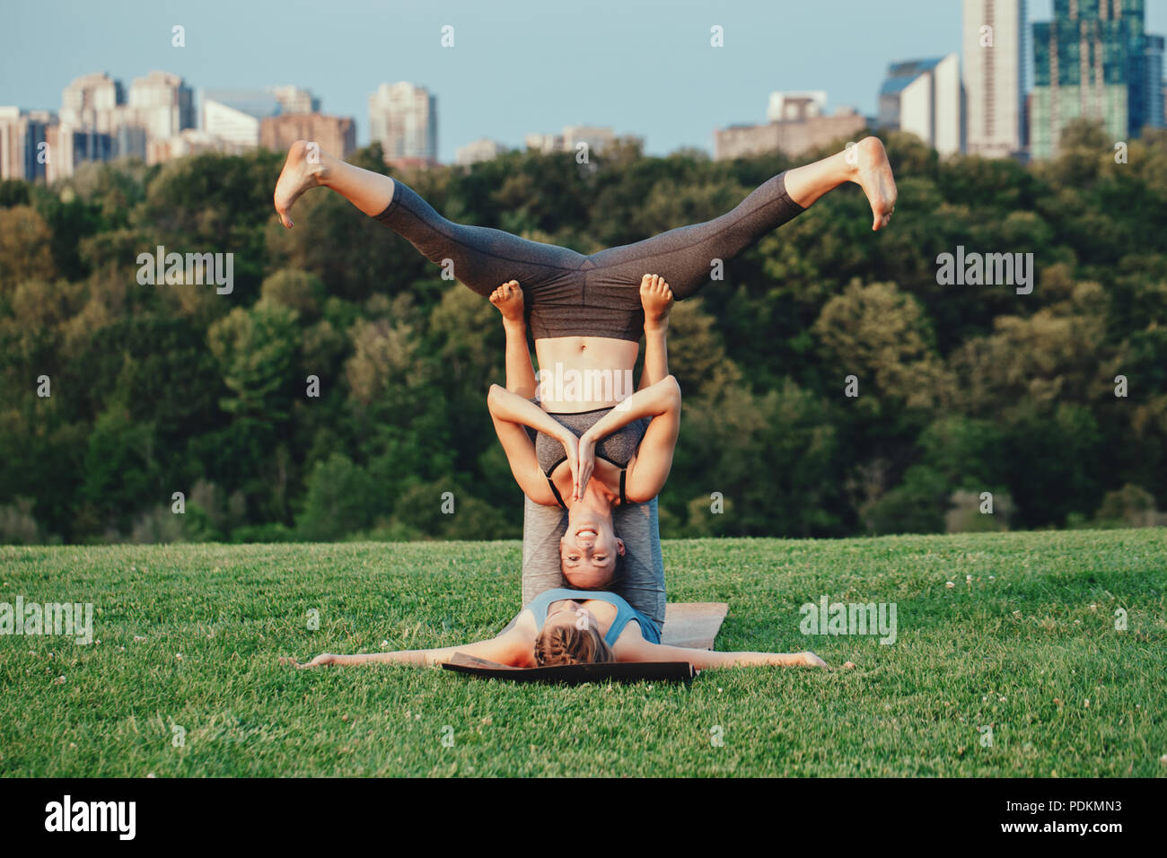 Two young beautiful Caucasian women yogi doing bat cartwheel acro yoga ...