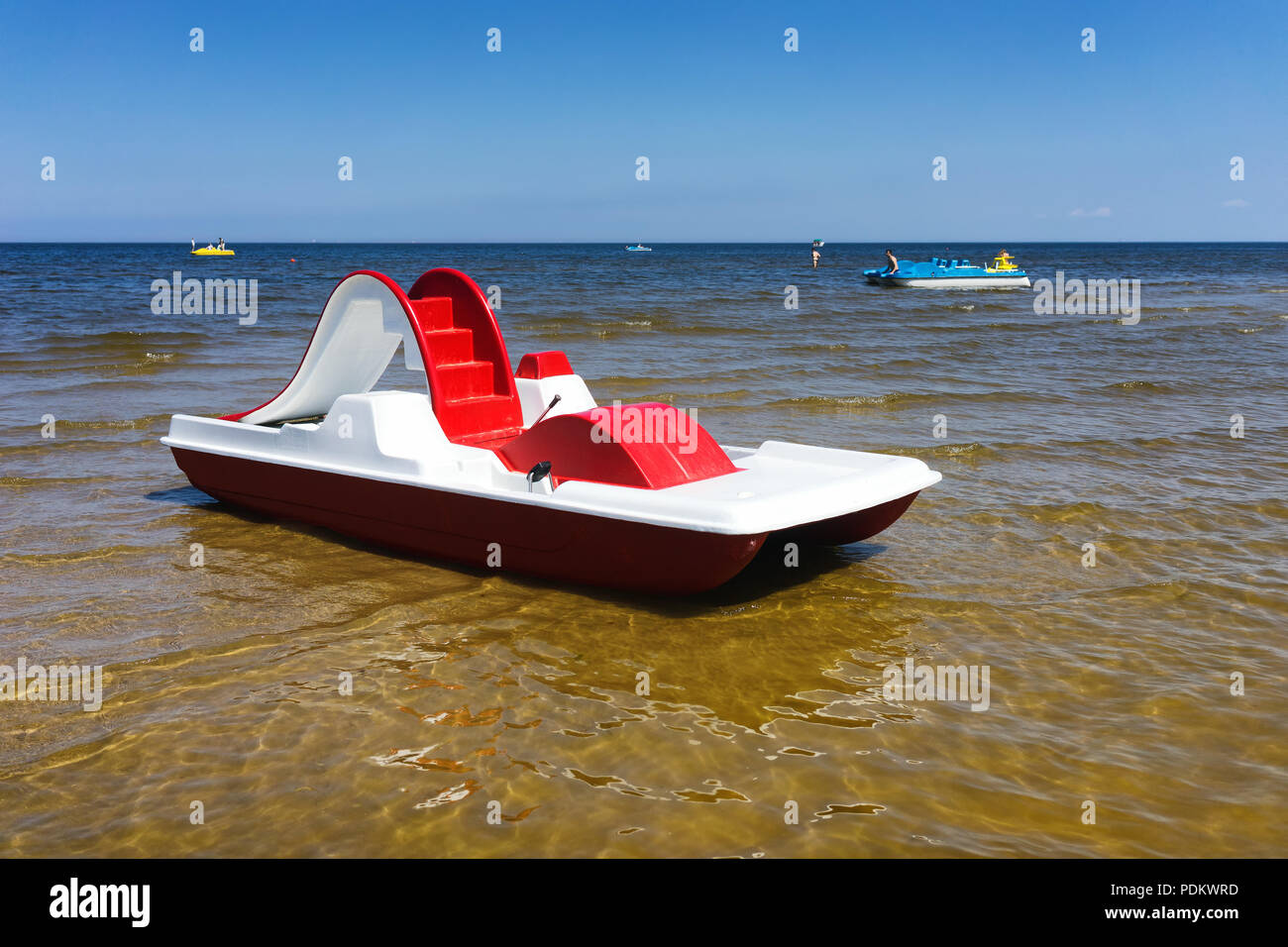 Red with a white top dinghy with pedals near the shore on the golden ...