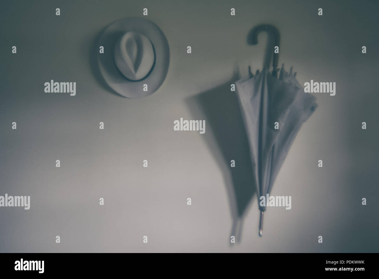 White umbrella with shadow and hat hanging on a nail in the wall ...