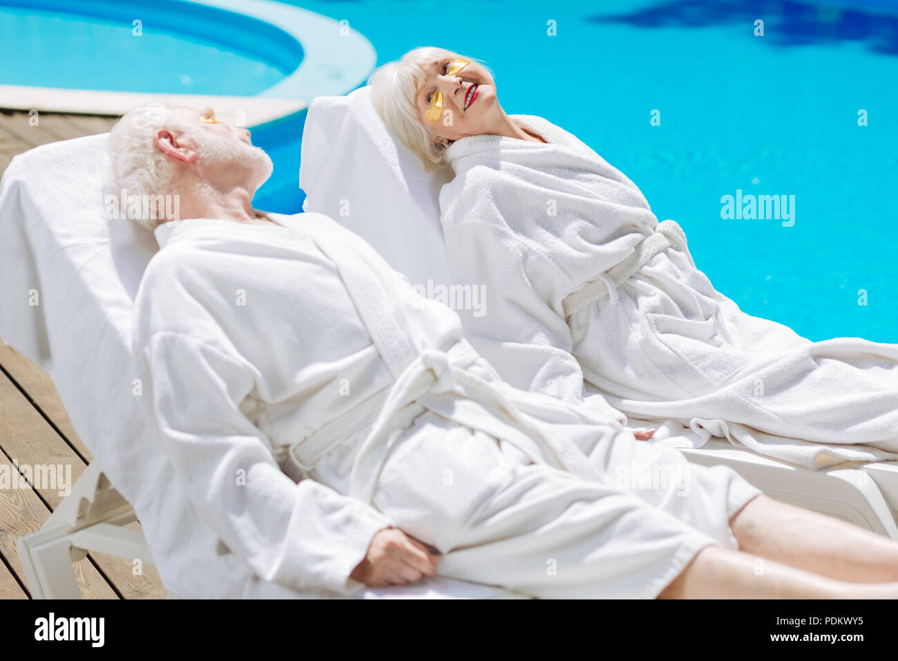 Retired man and woman wearing white bathrobes chilling near pool Stock ...