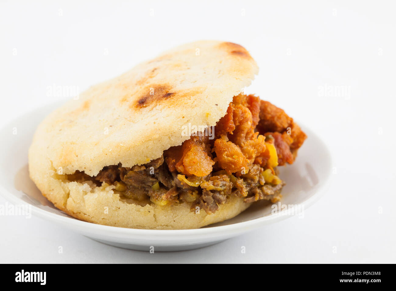 Arepas filled with shredded beef and pork rind served in white dish on ...