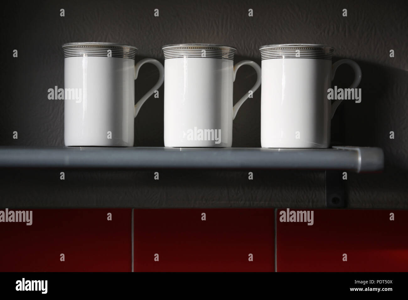 Three white coffee mugs lined up on a metal shelf Stock Photo - Alamy