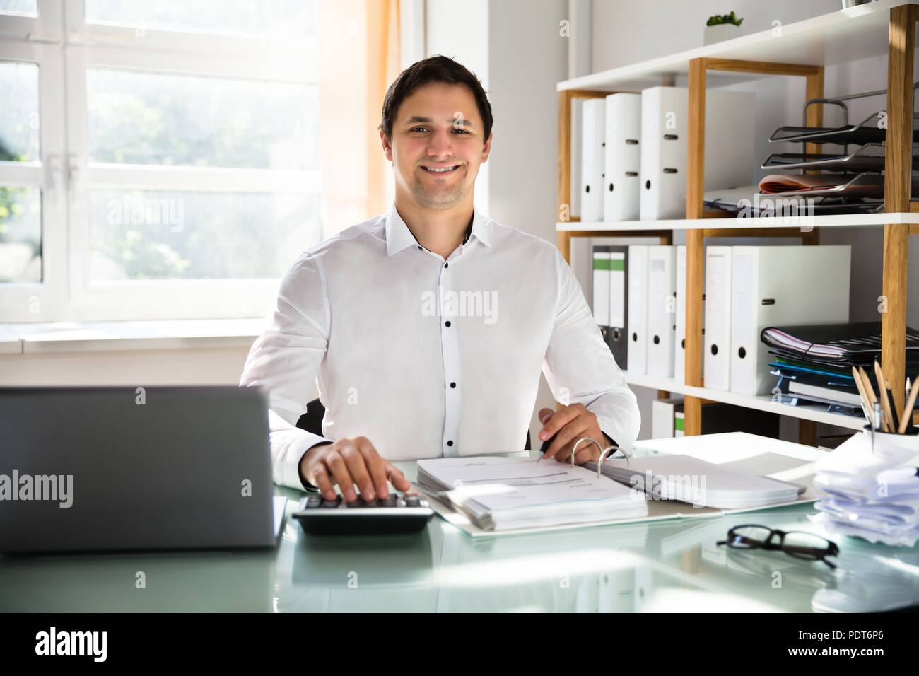 Portrait of a happy young businessman calculating invoice Stock Photo ...