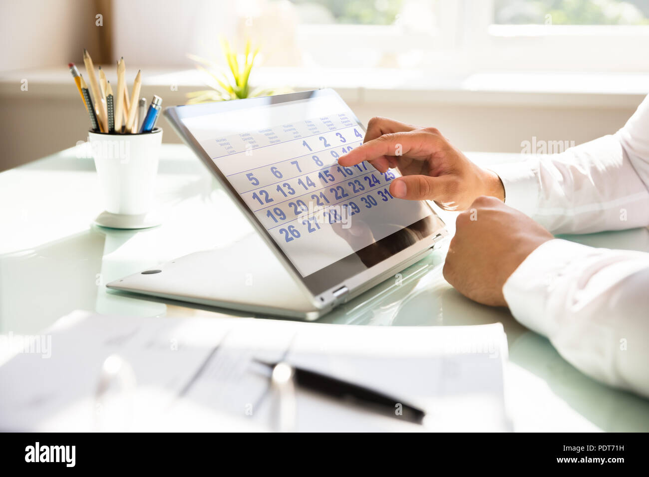 Close-up of a businessman's hand using calendar on laptop over desk ...