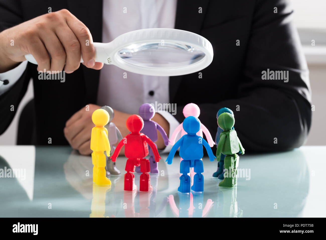 Businessperson's hand holding magnifying glass over multi colored human ...
