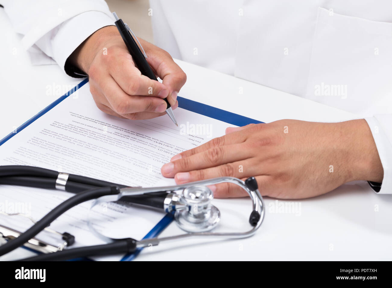 Doctor's hand signing document with stethoscope on desk Stock Photo - Alamy
