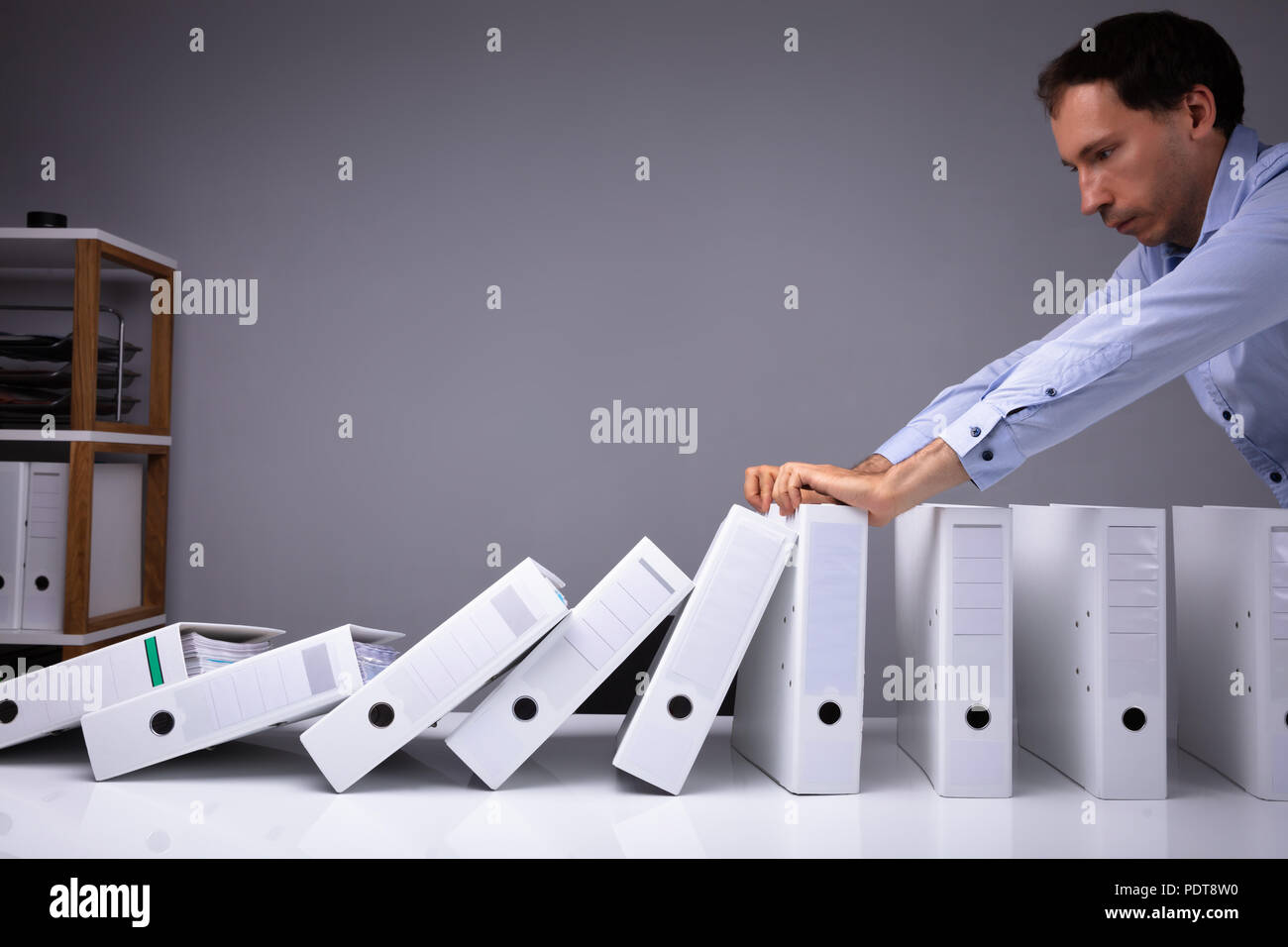 Man Stopping Falling Files On Desk In Office Stock Photo - Alamy