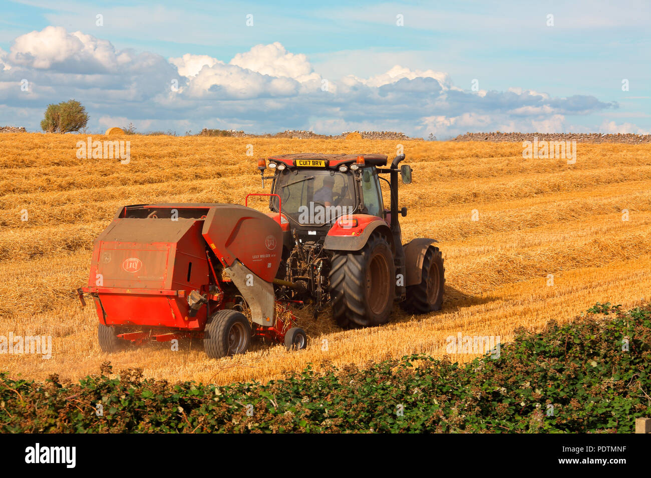 The local farmer in his tractor pulling along a baling machine to ...