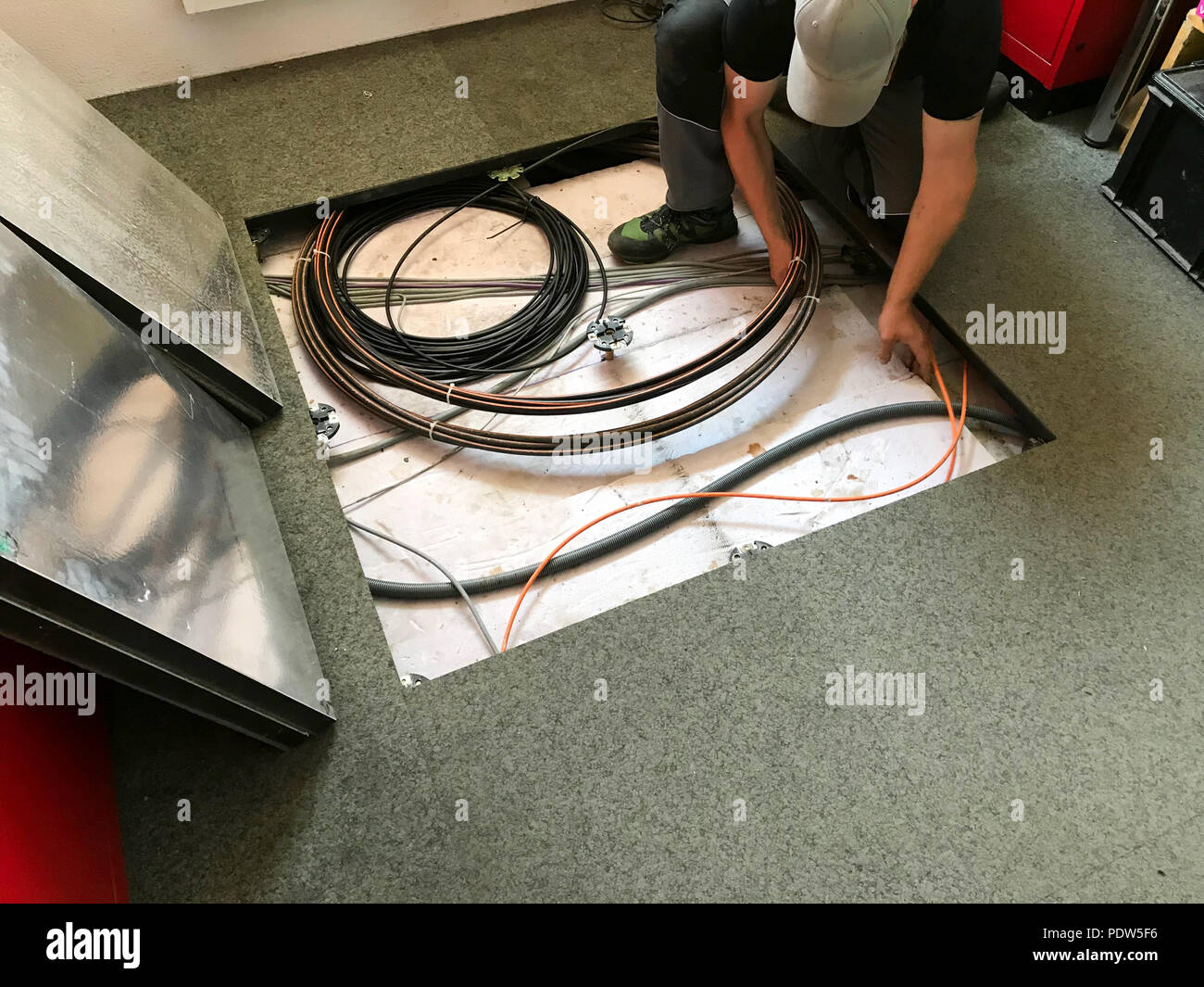 young male electrician working on cables in the subflooring and ...