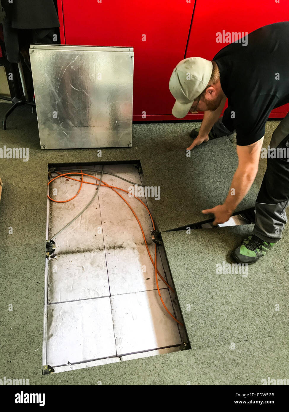 young male electrician working on cables in the subflooring and ...