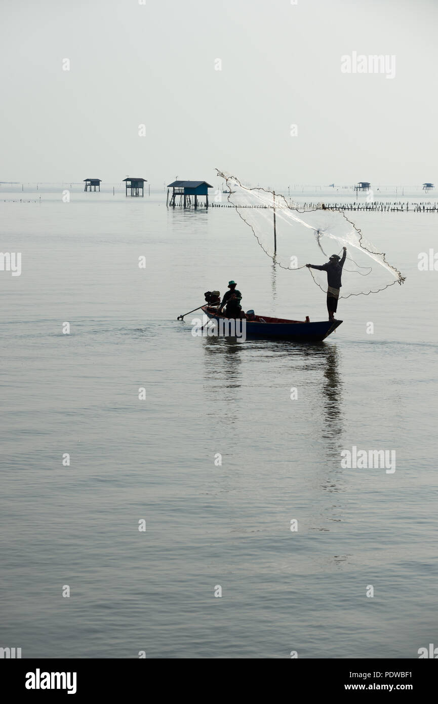 Fisherman on wooden boat casting a net for catching freshwater fish in ...