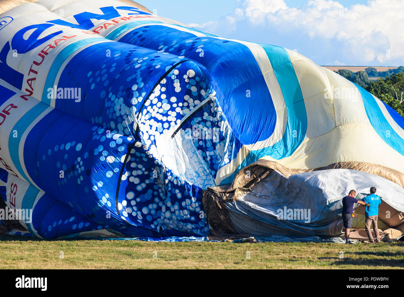 Large hot air balloon during inflation on ground with people for scale ...