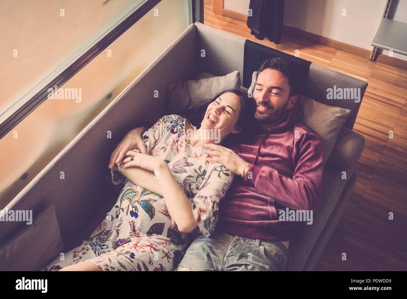 beautiful couple of models lay down on the sofa at home enjoying the ...