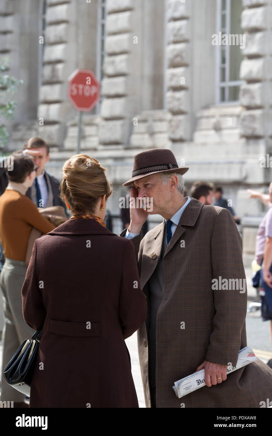 Film extras dressed in 1960s style clothing awaiting instruction before ...