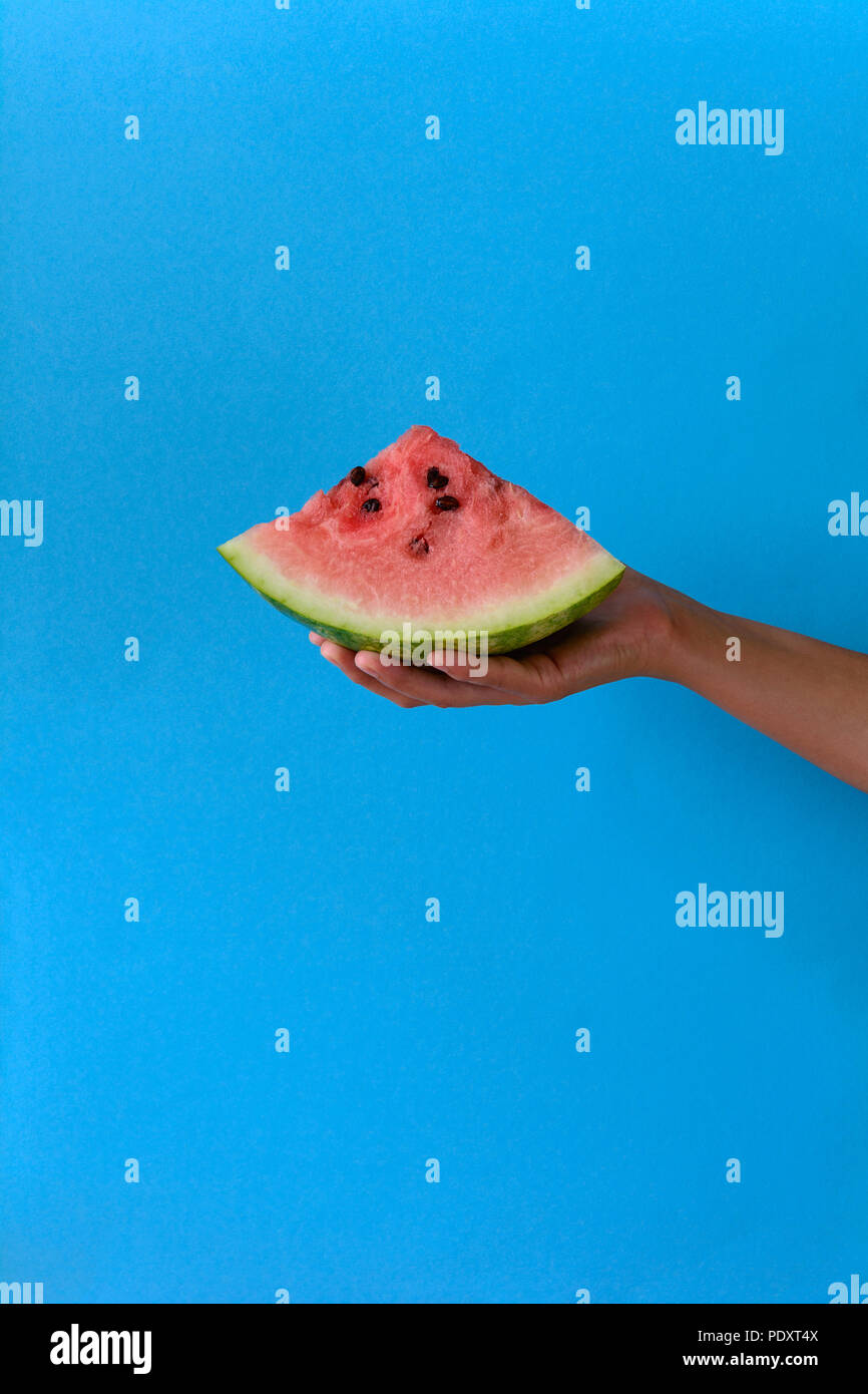 Hand holding watermelon slice on blue background Stock Photo - Alamy