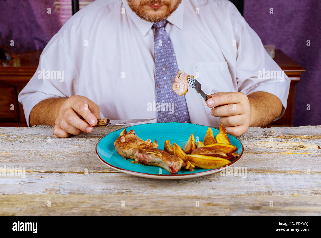 Portrait of man eating strip steak served with loaded baked potato with ...