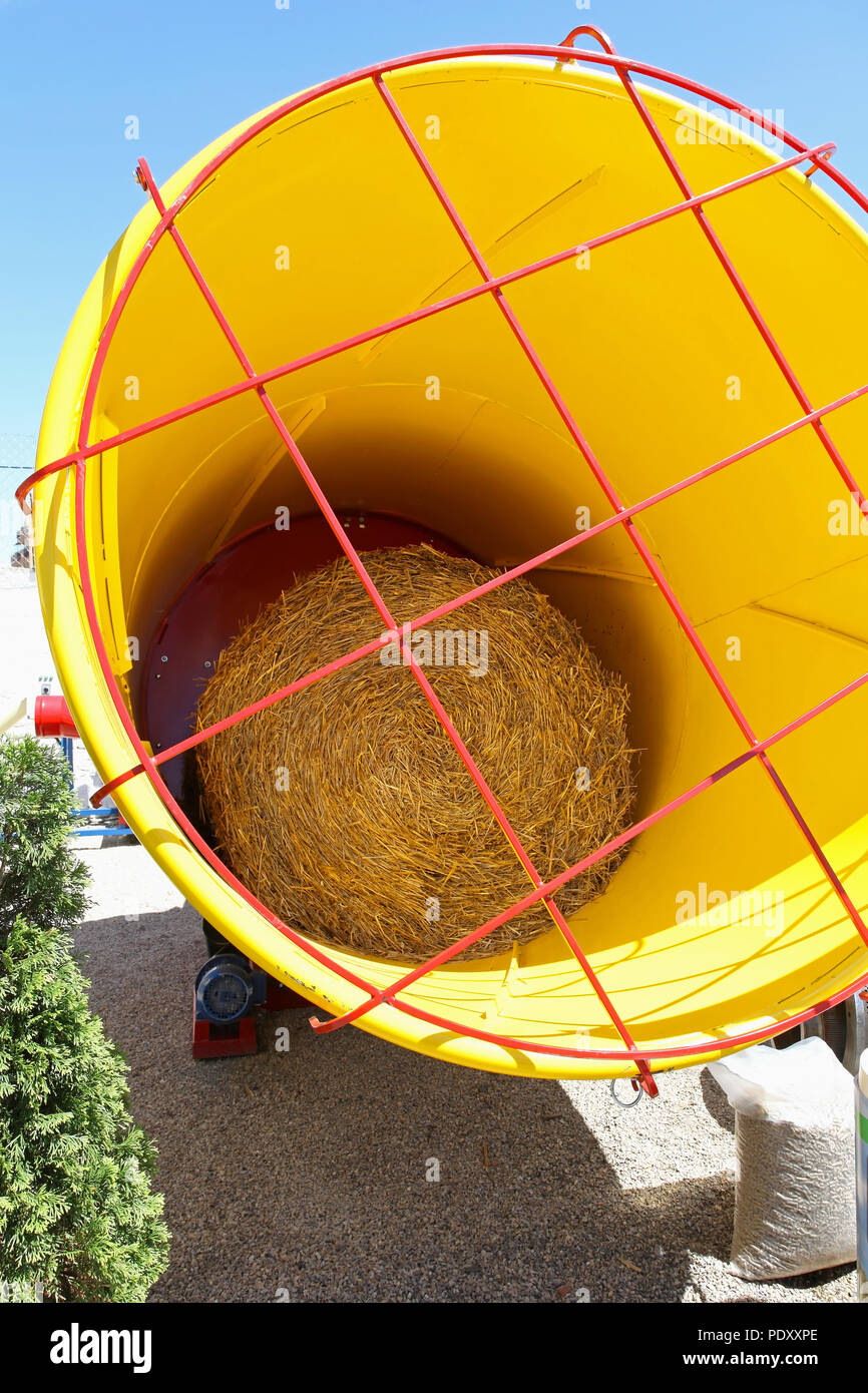 Straw bale roll in yellow rolling machine Stock Photo - Alamy