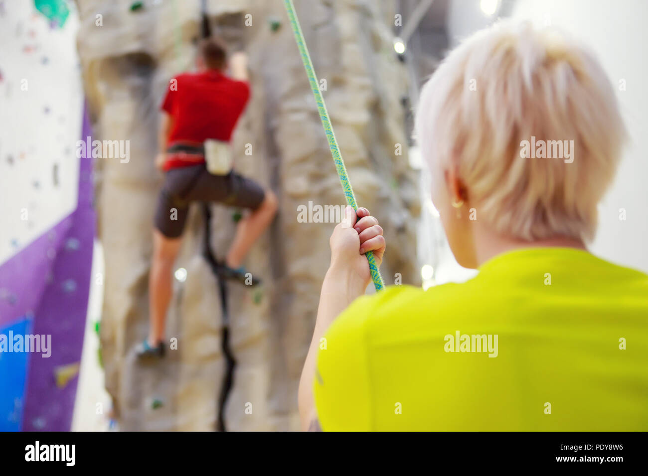 Photo from back of man clambering over climbing wall and female trainer ...