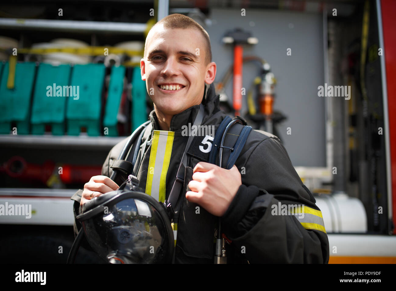 Photo of happy firefighter standing near fire truck with fire hose ...