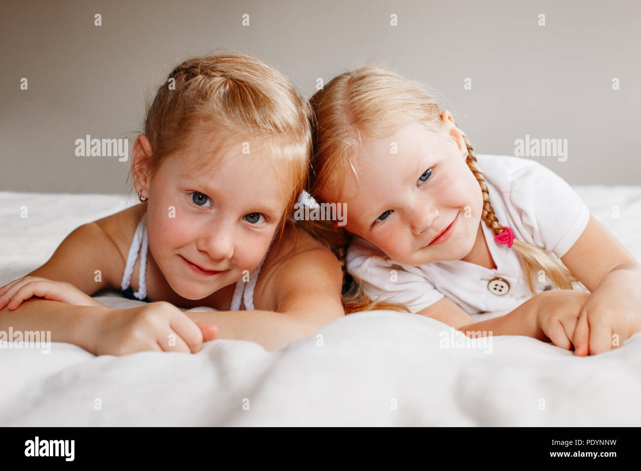 Closeup portrait of two cute adorable little red-haired blonde Caucasian girls sisters lying ...