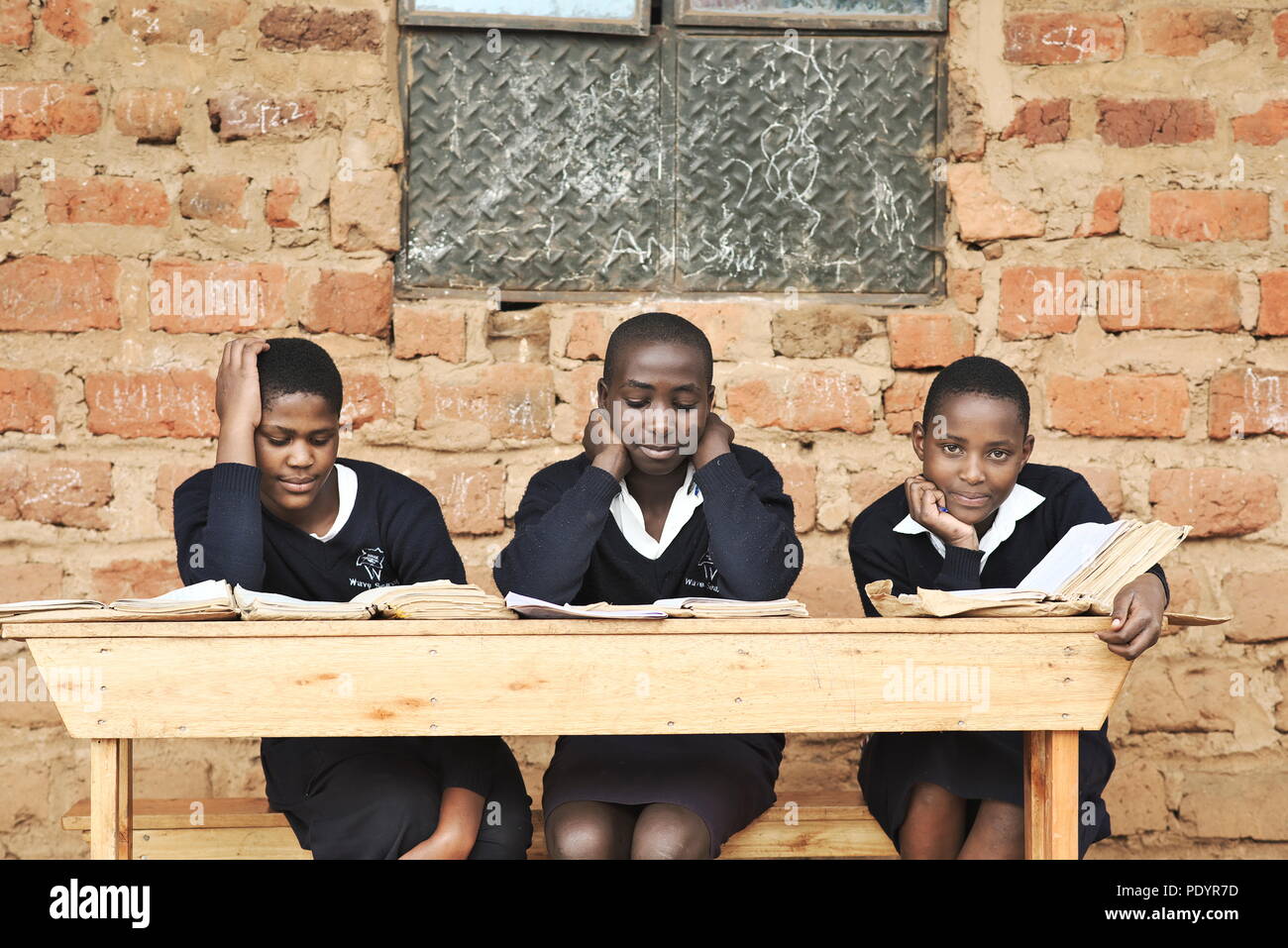 young Ugandan school children dressed in a school uniform sit outside ...