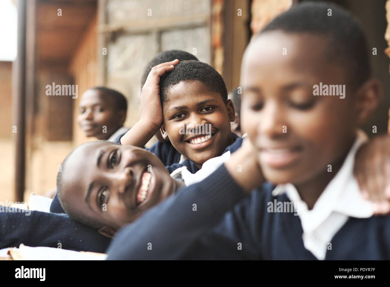 young Ugandan school children dressed in a school uniform sit outside ...