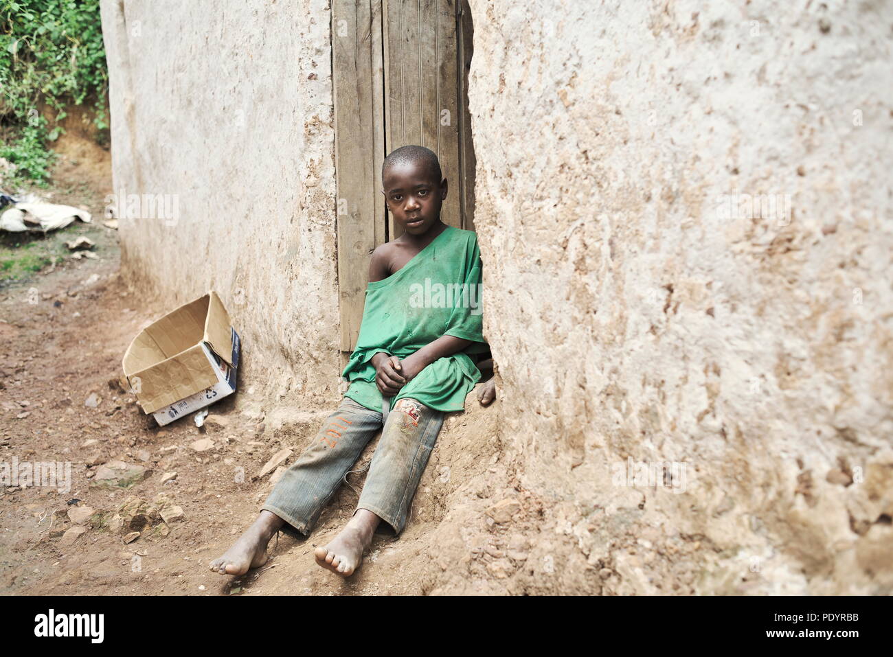 a poor under dressed Young Ugandan child sits in a doorway of a ...