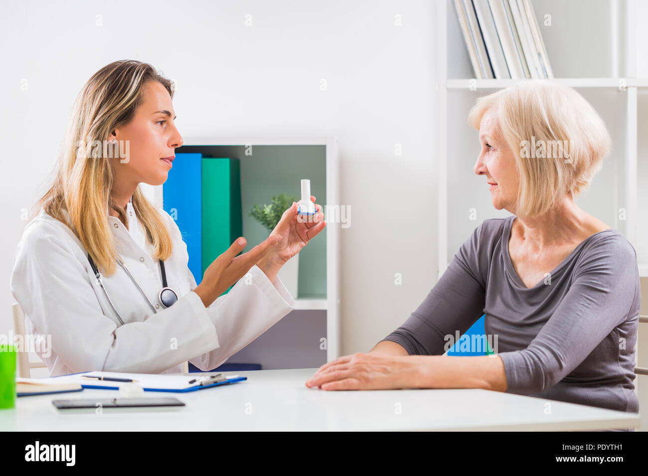 Female doctor is explaining how to use inhaler to her senior woman ...