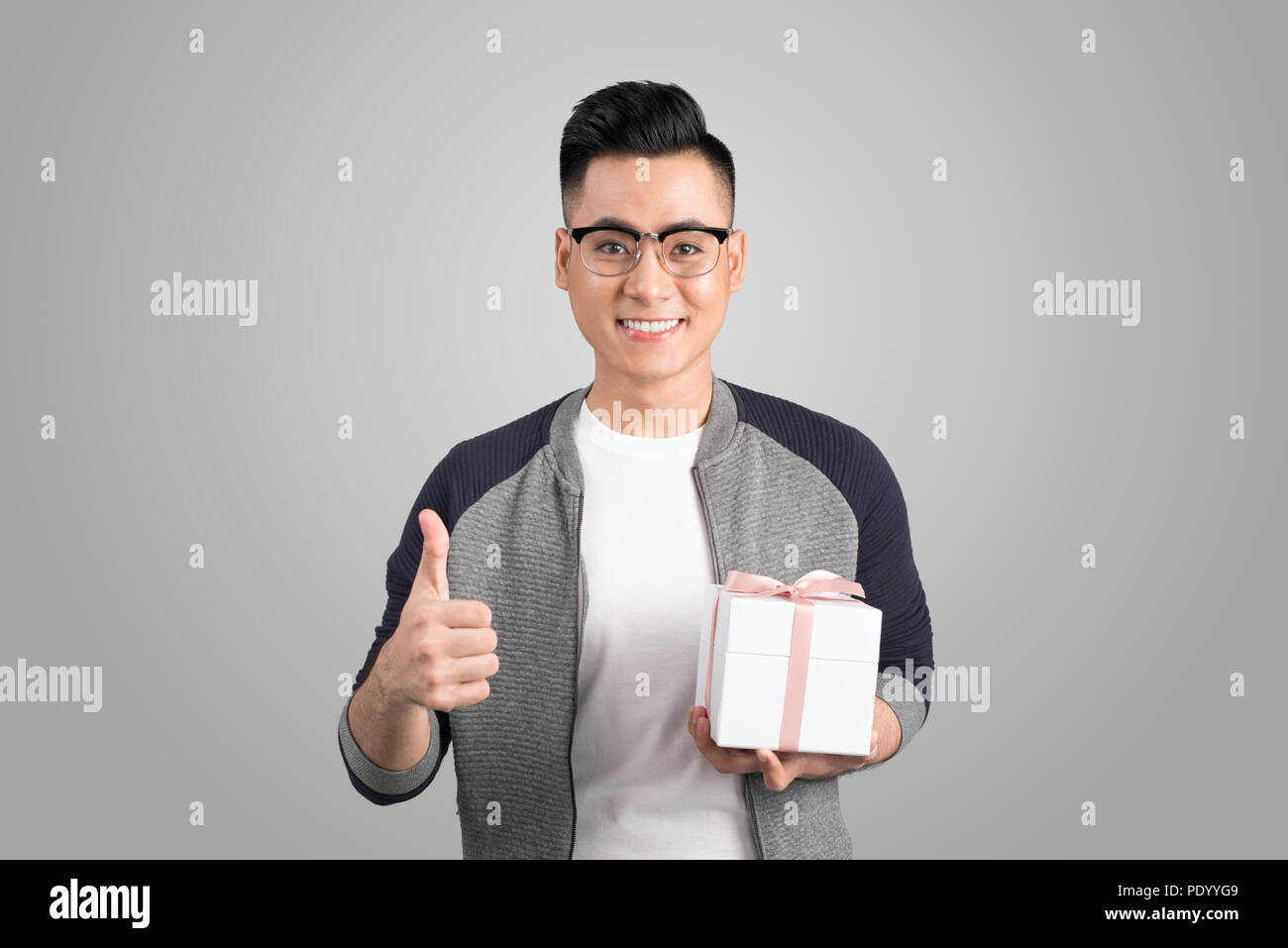 Asian man thumbs up and holding gift box. Studio shot, gray background ...