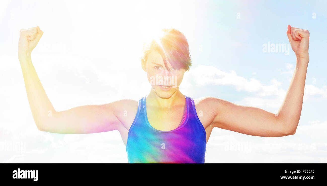 young woman flexing her muscles in front of sunny blue sky Stock Photo ...