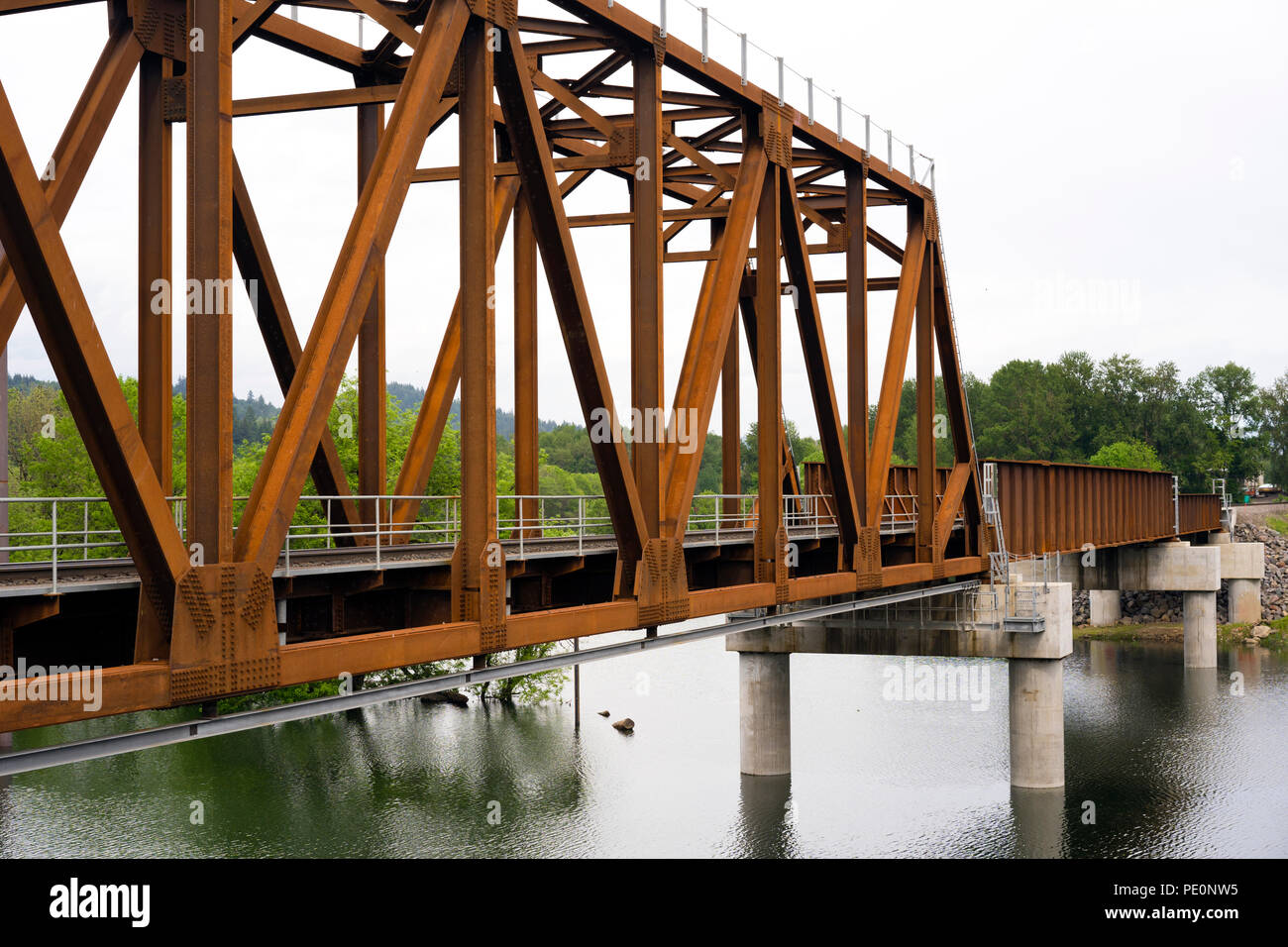 A new unpainted rusted metal truss railway bridge on concrete piles ...