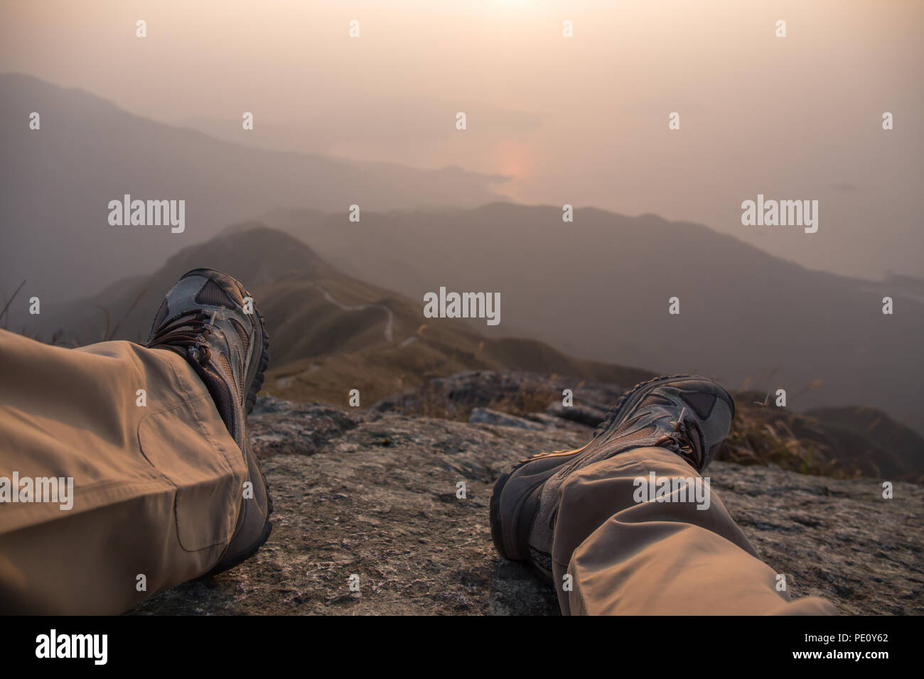feet and leg of hiker sit on peak with hiking trail and mountain range ...