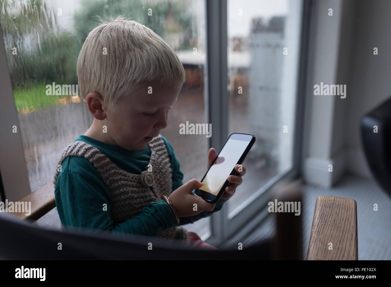 Boy using mobile phone while sitting on chair Stock Photo - Alamy