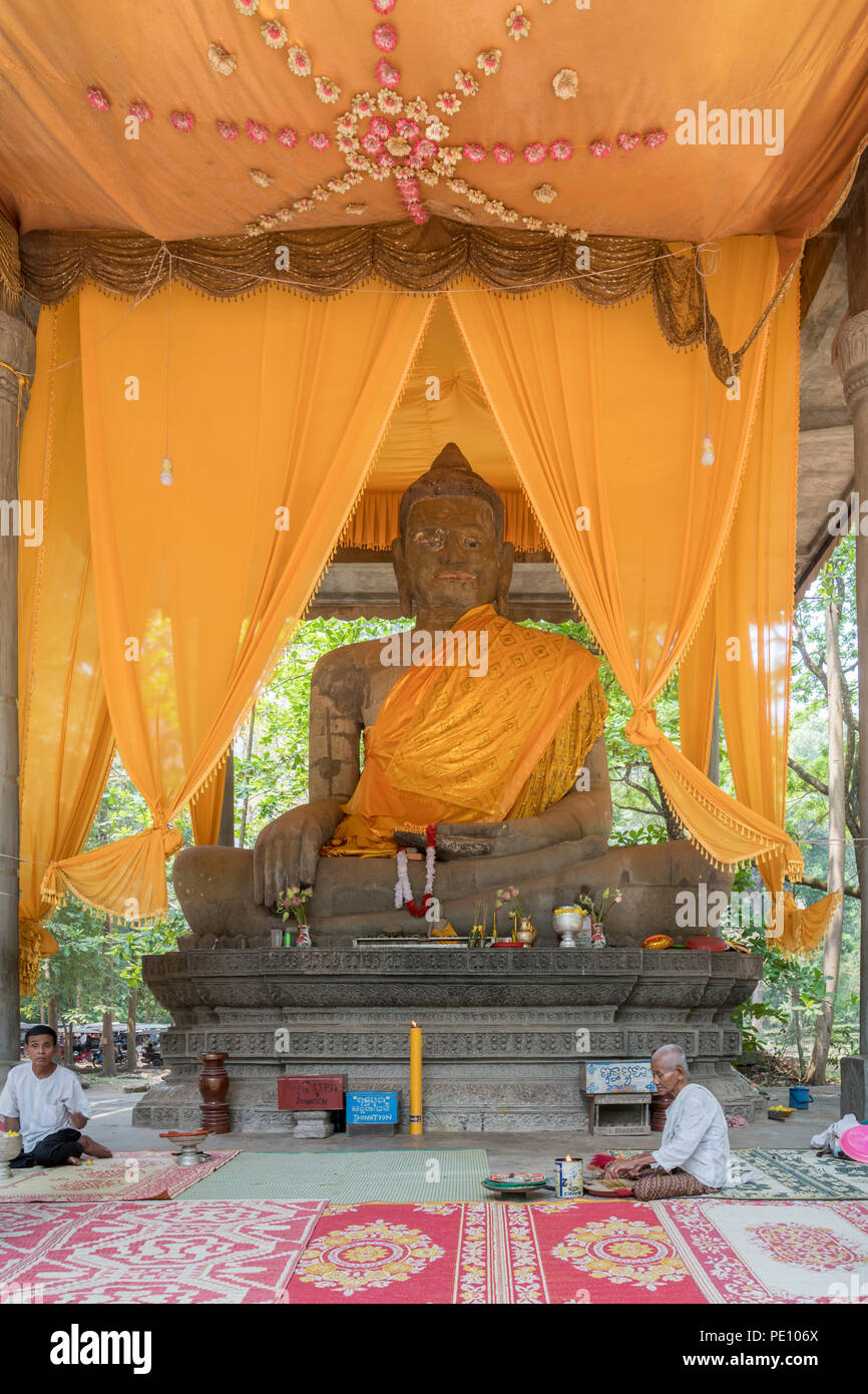 Worshippers praying in front of a large statue of Buddha sitting ...