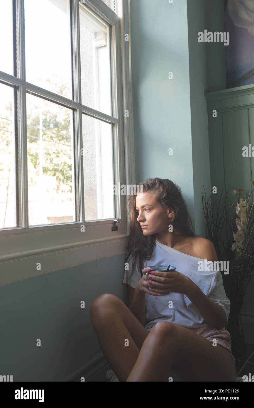 Woman sitting near window while having coffee Stock Photo - Alamy
