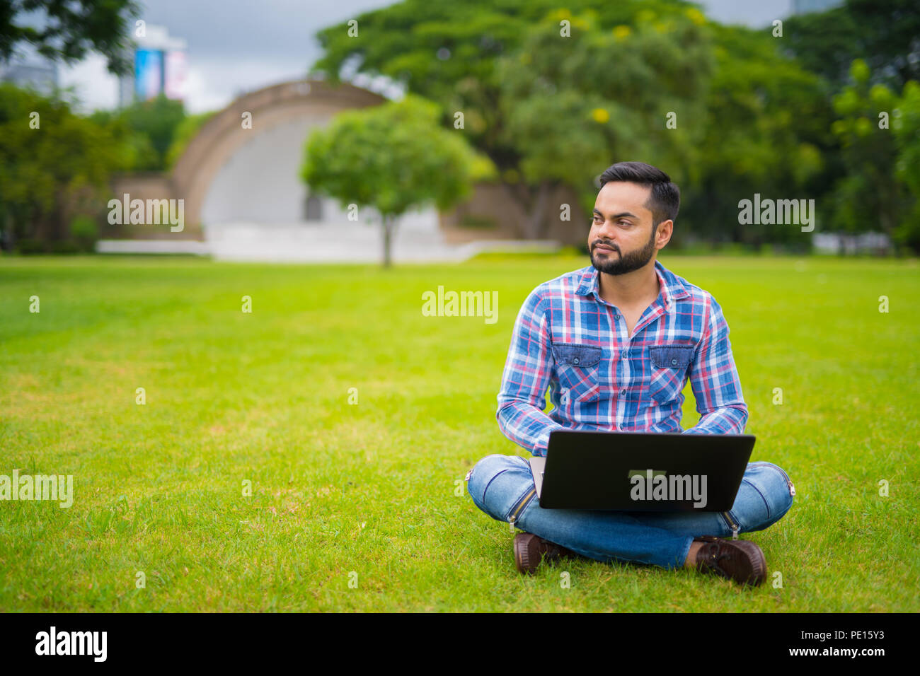 Indian Man In Park Using Laptop Computer And Thinking Stock Photo - Alamy