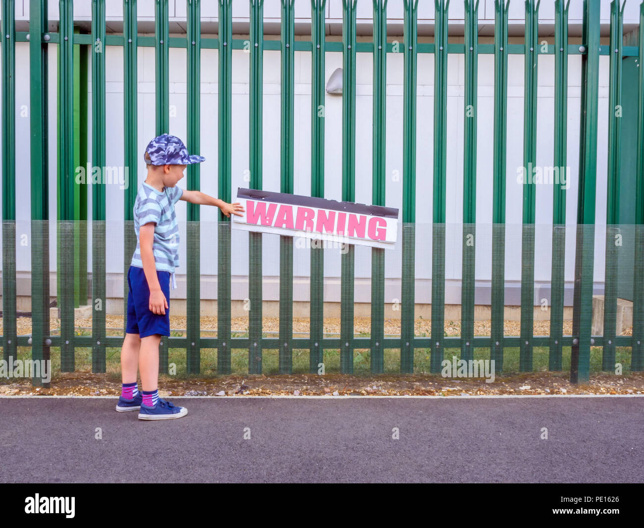 Day view little child boy touching warning sign on green metal fence in ...