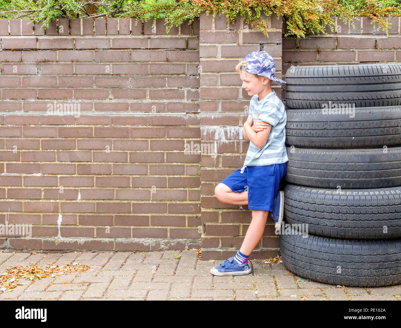 Day view cute little child boy posing next to stack of used tyres over ...