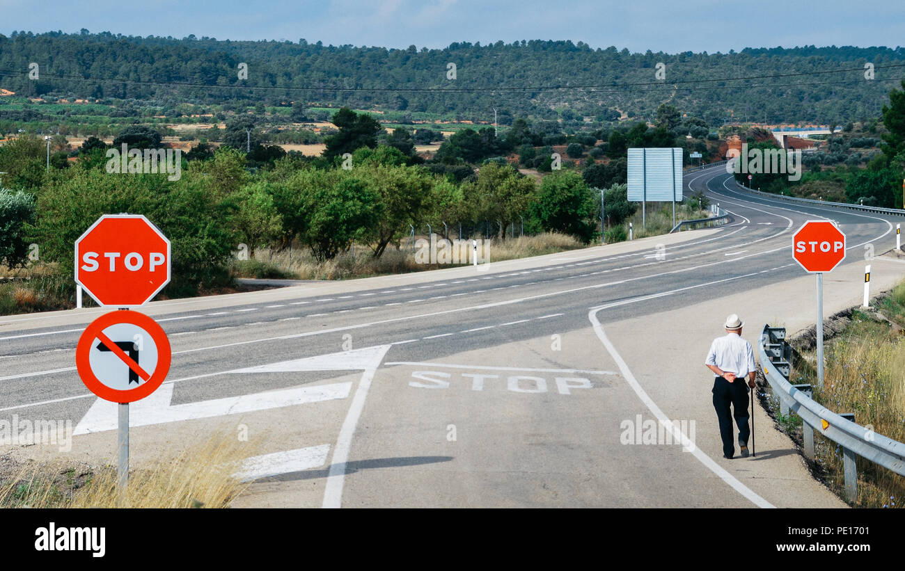 Elderly man walking with a cane past a red stop sign leading to a ...