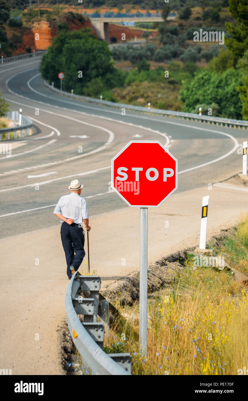 Elderly man walking with a cane past a red stop sign leading to a ...