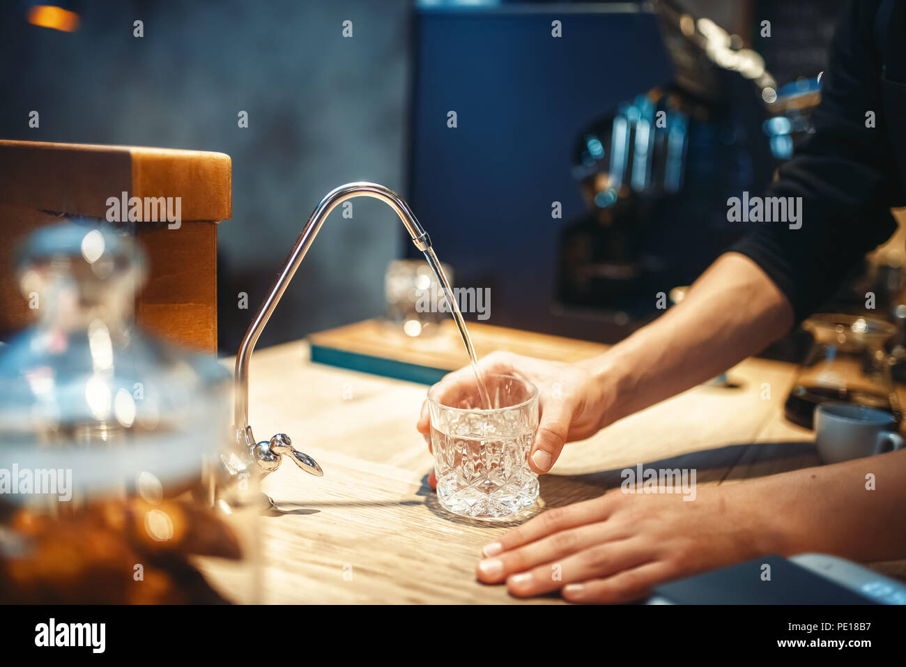 Male barista pours filtered water into the glass, cafe or bar counter ...