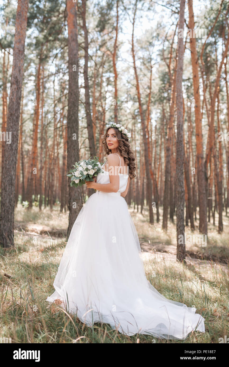 A cute curly woman in a white wedding dress with a wedding bouquet and ...