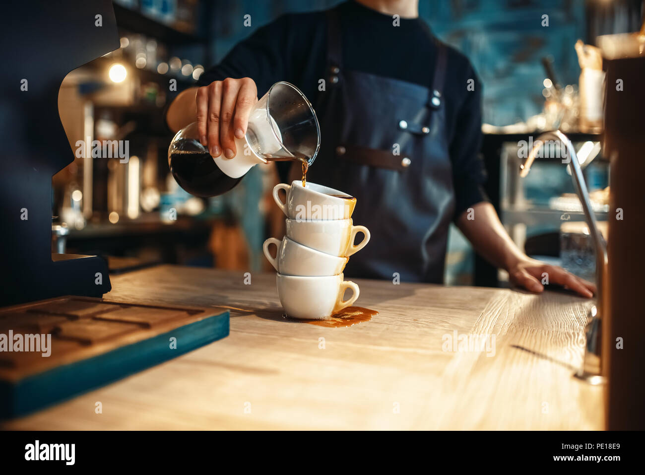 Male barista pours black coffee on a stack of cups, cafe counter and ...